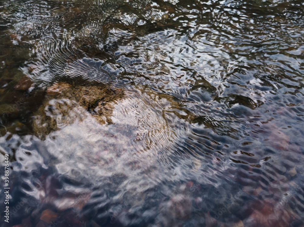Wavy surface of water on shallow rapid stream with colorful gravel at ...