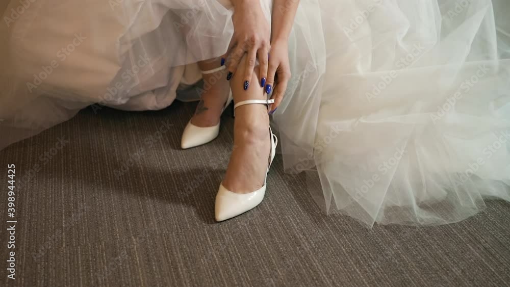 Low angle: Bride's hands touch legs while putting on white wedding ...