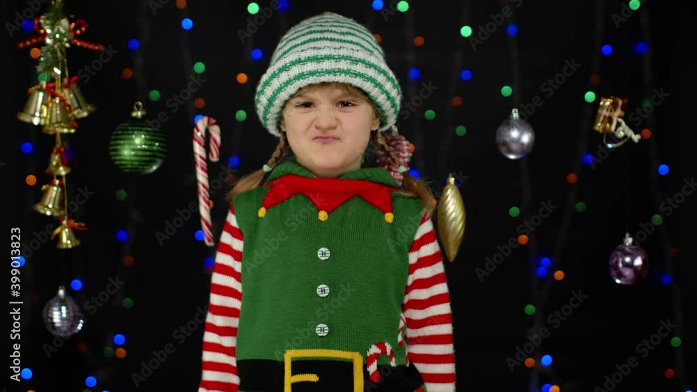 Displesed funny kid girl in elf Santa helper costume has spoiled mood ...