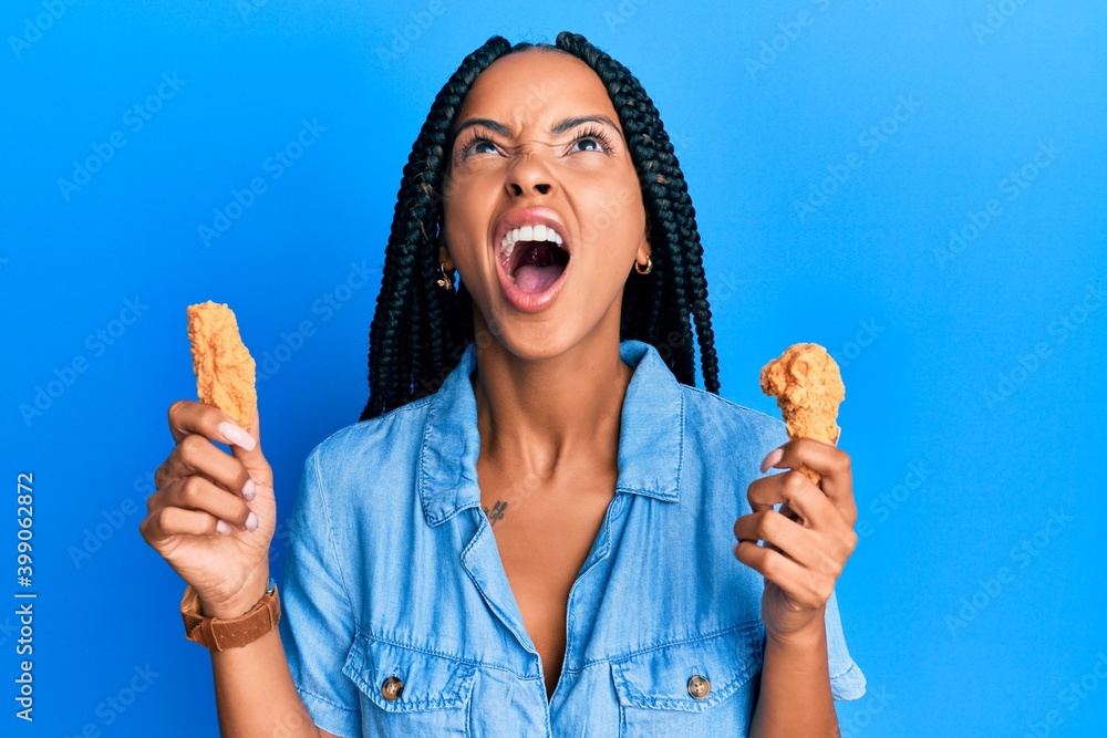 Beautiful hispanic woman eating chicken wings angry and mad screaming ...