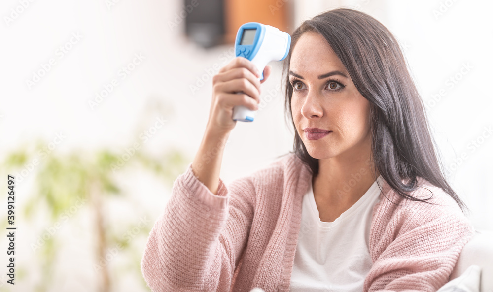 Woman self-measuring temperature with an infrared digital thermometer ...
