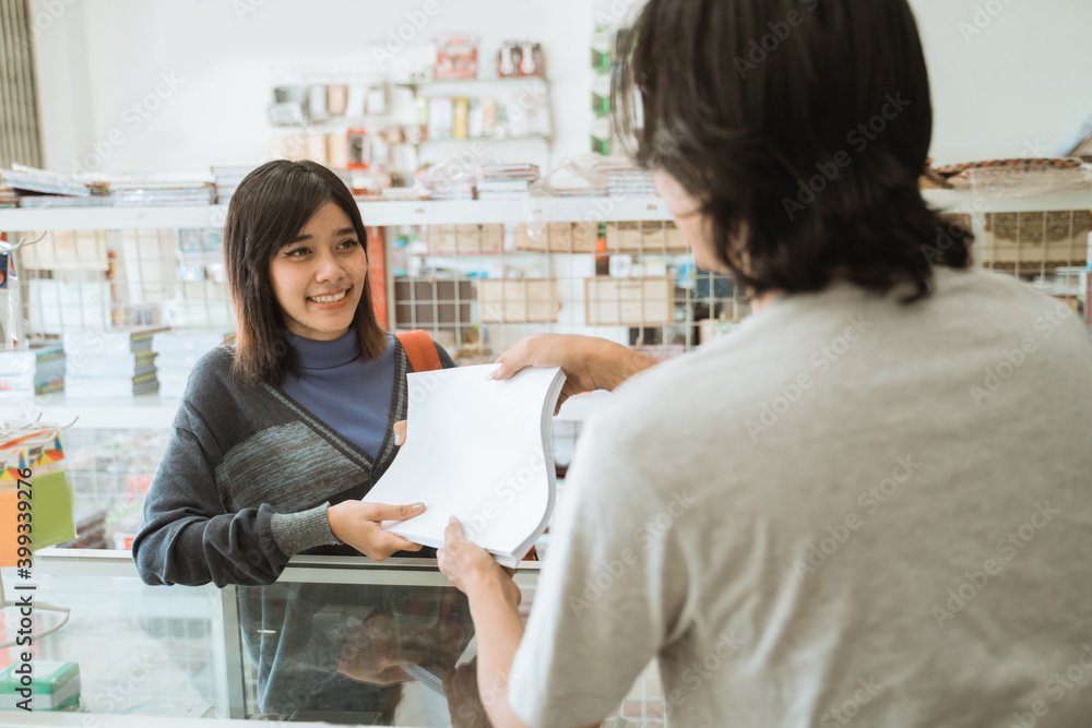 Young girl visiting a stationery shop talks to a male cashier buying ...