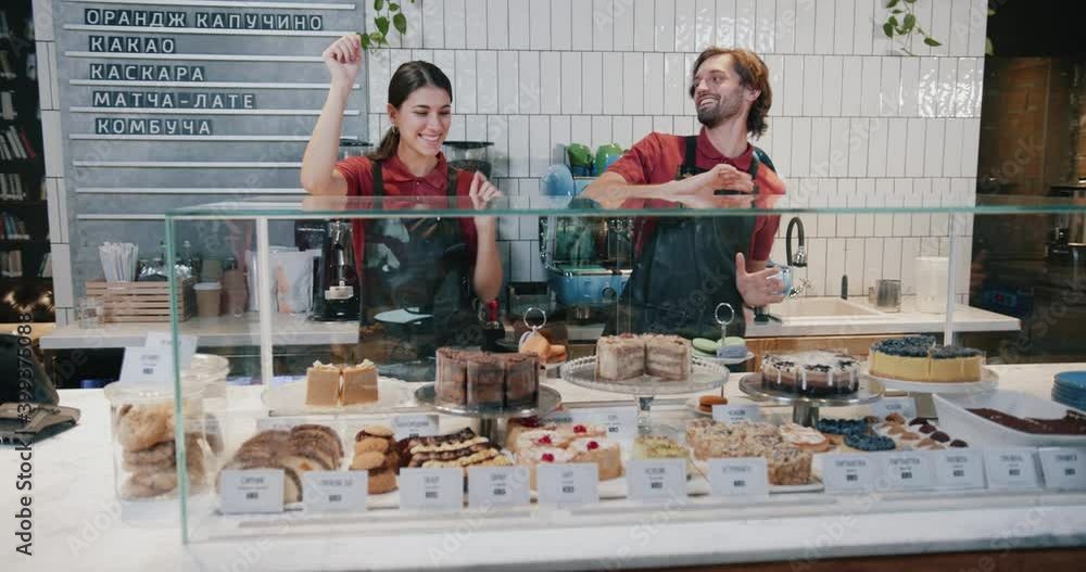 Cheerful team of malebarista and female cashier dancing at bar counter ...