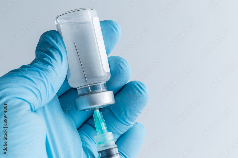 One gloved hand holding a vial containing a vaccine and a hypodermic ...