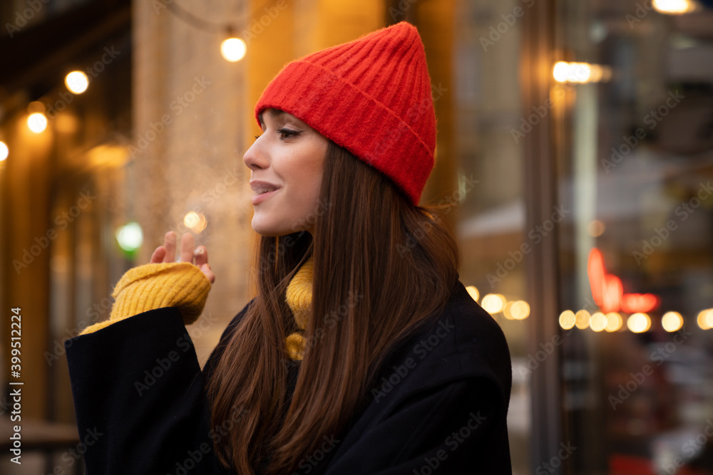 Charming happy girl smiling and smoking while standing at city street ...