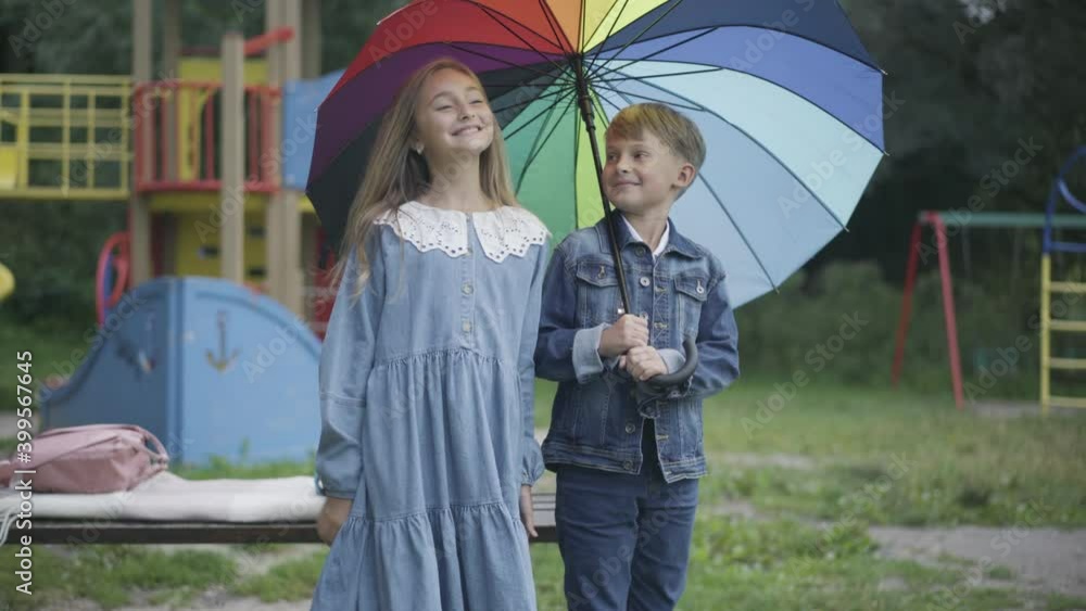 Joyful Caucasian girl kissing boy on cheek. Shy cute schoolboy holding ...