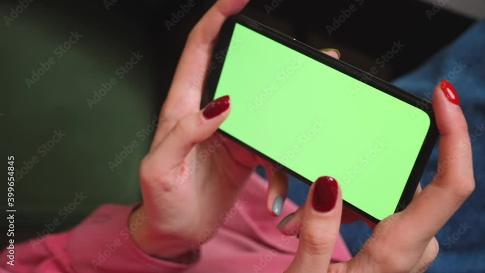 Close up woman hands holding chromakey green screen smartphone watching content, swiping ...
