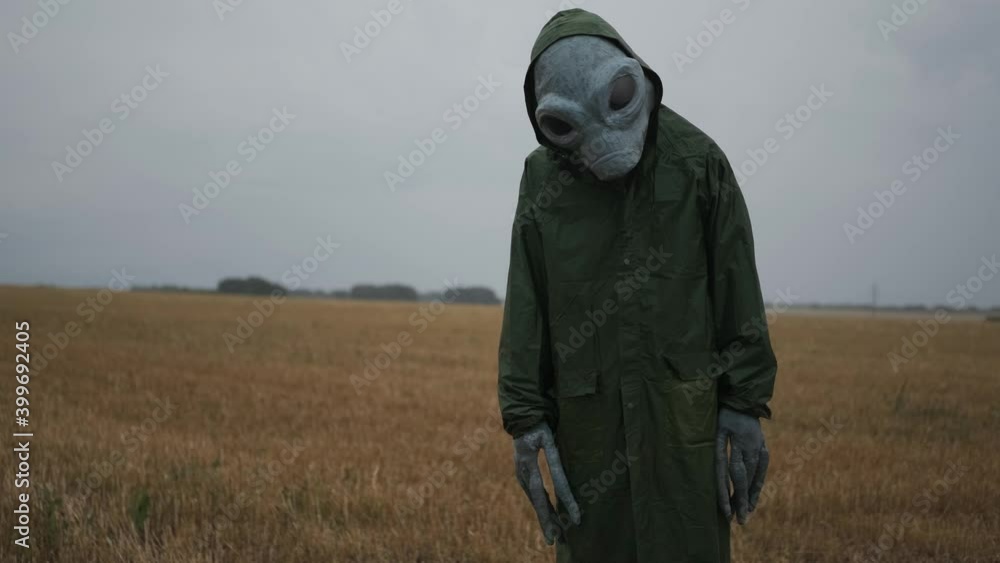 an alien in green suit stands alone in field, looks around, waves his ...
