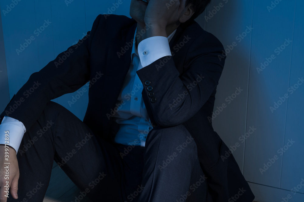 暗い部屋で床に座り込んだビジネスマン Photos | Adobe Stock