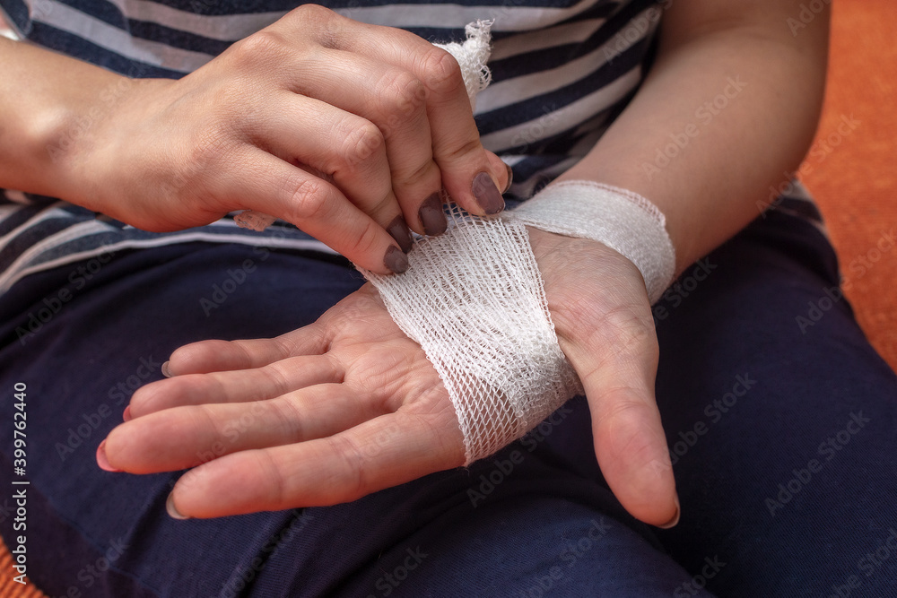 The girl is bandaging her wounded palm and wrist while sitting on the ...
