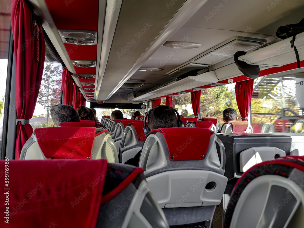 Passengers ride in the cabin of a modern bus with red curtains and ...