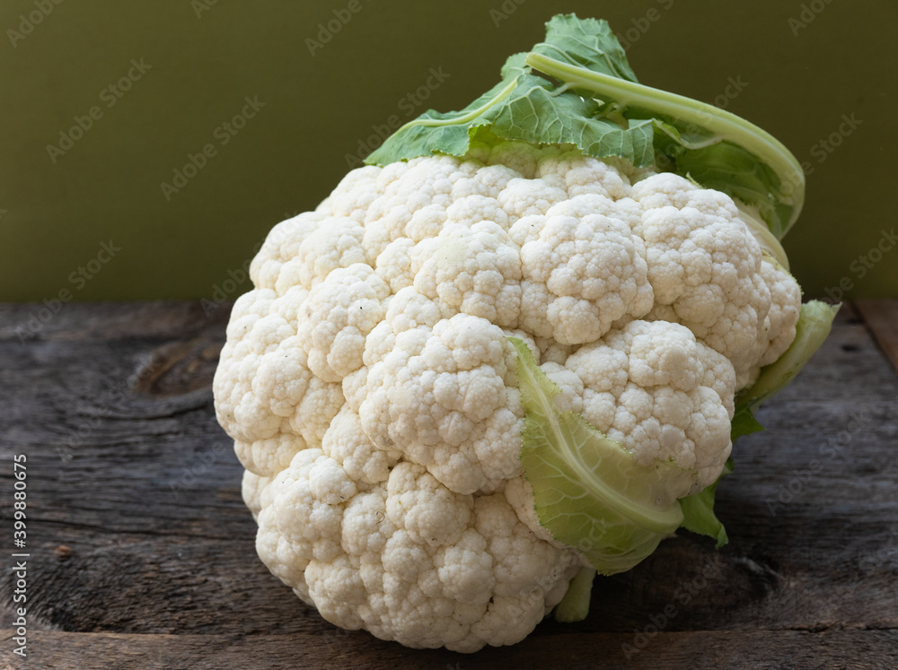 Single head of cauliflower with leaves on barn wood with green ...