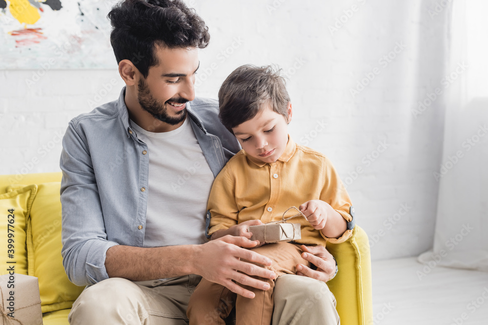Smiling hispanic father embracing son with gift box at home, two ...