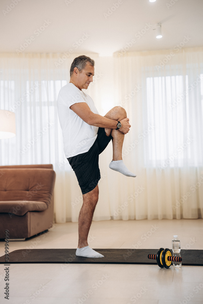 Mature man standing on one leg and stretching another. Workout on black ...