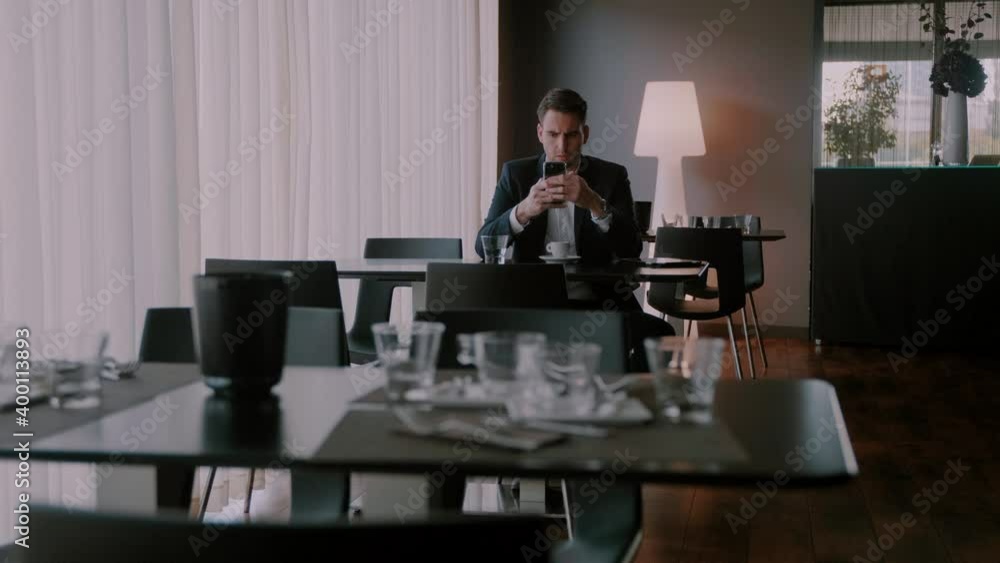 Businessman sitting at an empty table and typing on a phone infront of ...