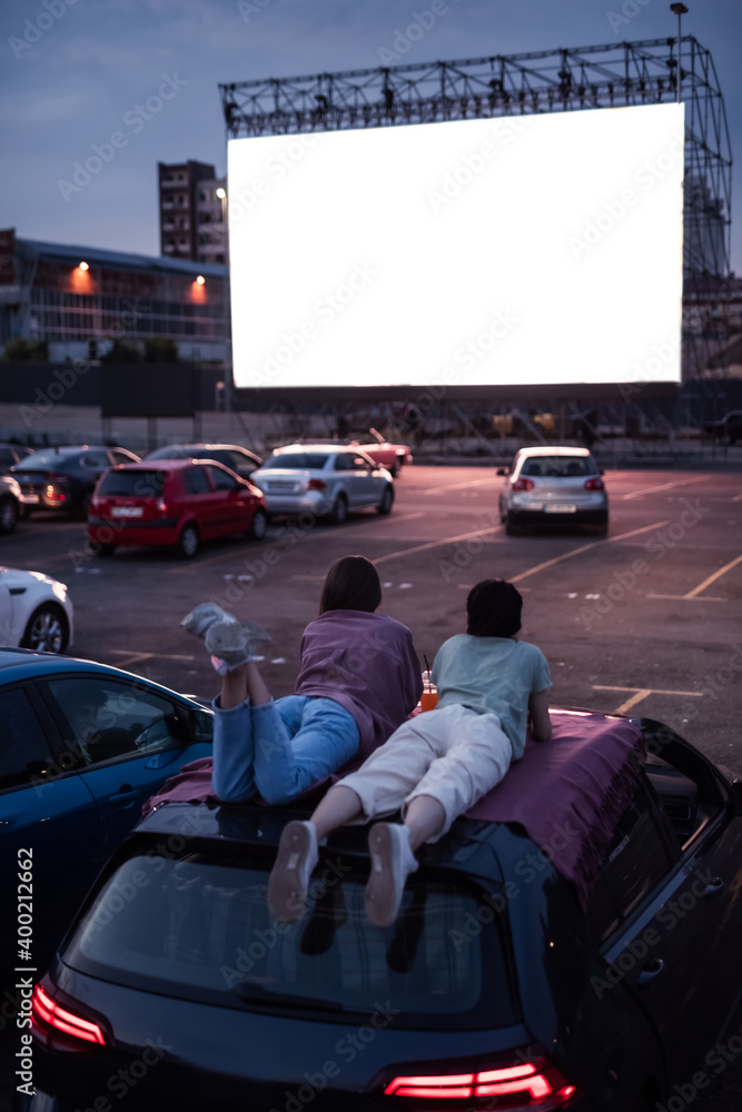 Enjoy the movie. Rear view of two friends lying on the roof of a car ...