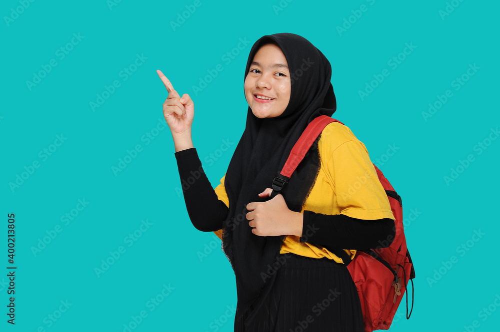 Portrait of teenager muslim female student in hijab pointing at copy ...