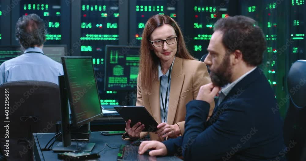 Two programmers work together in server room at desktop: woman holds ...