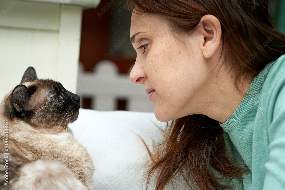 Beautiful woman looking at her cat sitting on a coach at home. concept ...