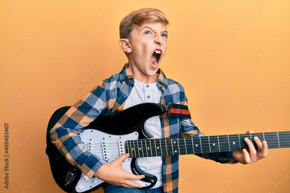 Little caucasian boy kid playing electric guitar angry and mad ...