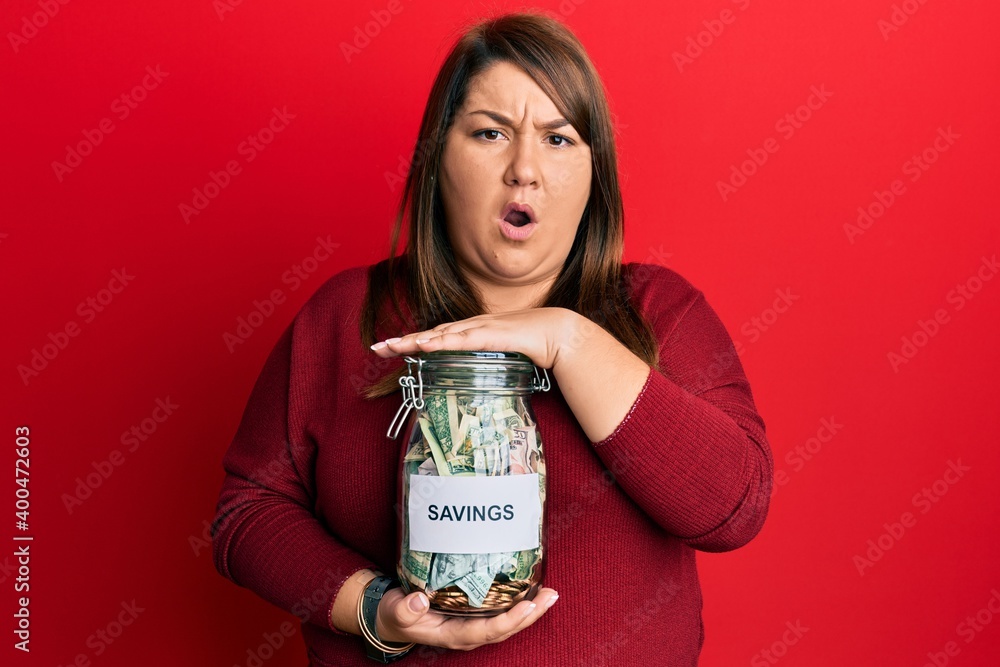 Beautiful brunette plus size woman holding jar with savings in shock ...