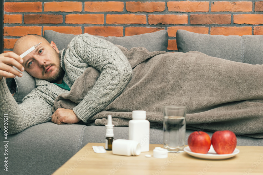 Sick man on sofa measure body temperature, check a thermometer, guy is ...
