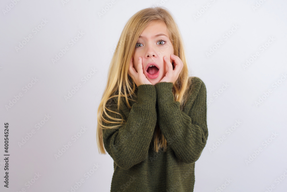 Stupefied Caucasian kid girl wearing green knitted sweater against ...