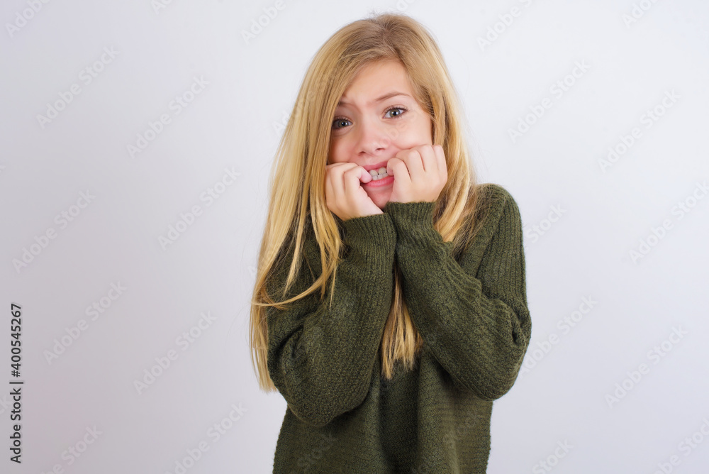 Fearful Caucasian kid girl wearing green knitted sweater against white ...