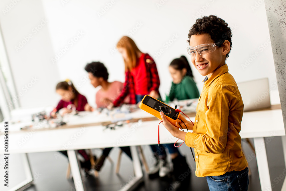 Cute little boy standing in front of kids programming electric toys and ...