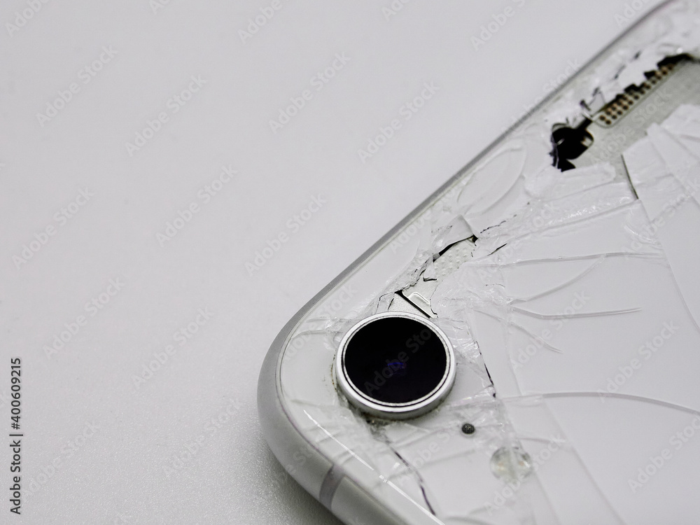 The back of modern white smartphone with a broken glass and a damaged ...