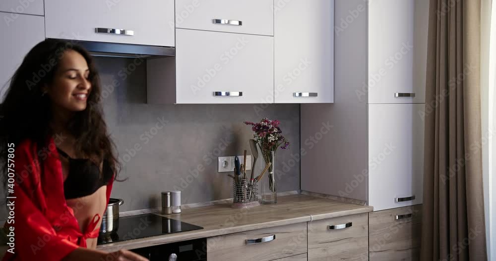 Happy alluring young woman dancing in her kitchen in a flowing red ...