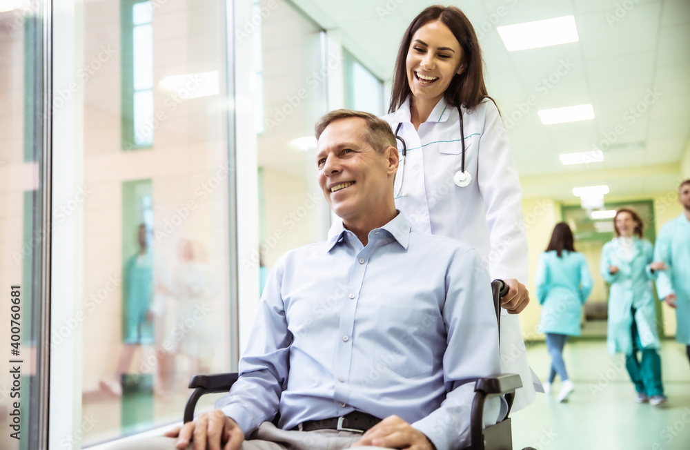 Senior handsome man in a wheelchair is moving in the hospital with help ...
