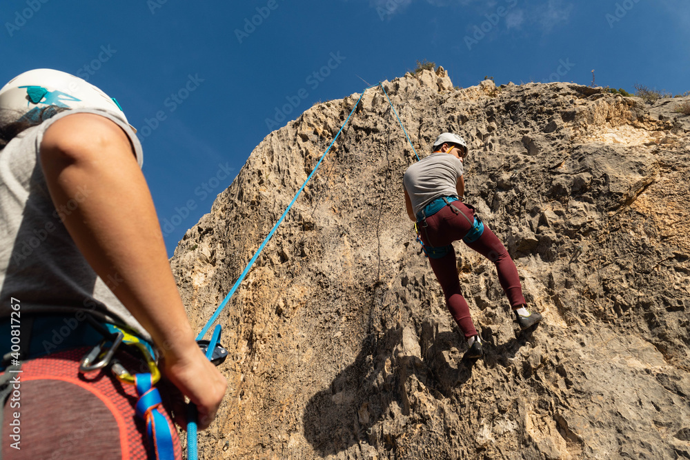 View from the back of the girl climber who is lowering a boy climber ...