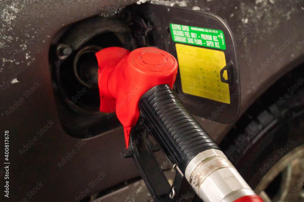 Red refueling gun in the fuel tank of a dirty, snowy car at a gas ...