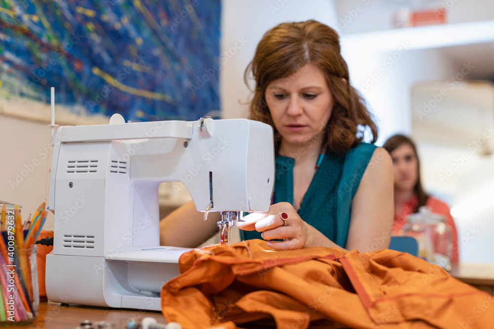 Female seamstress sewing orange fabric on machine at fashion studio ...