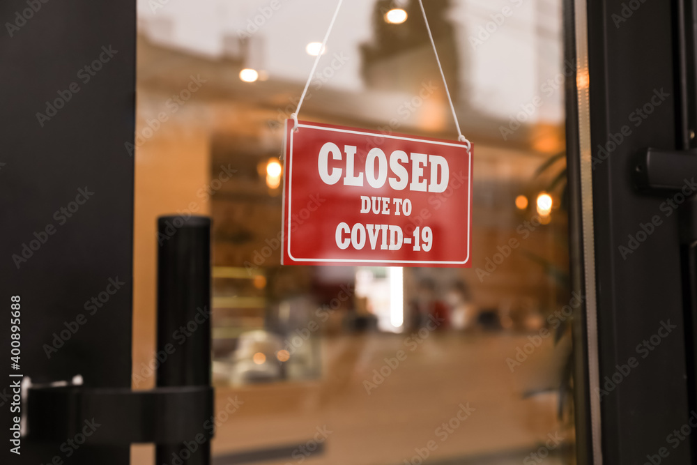 Red sign with words "Closed Due To Covid-19" hanging on glass door ...