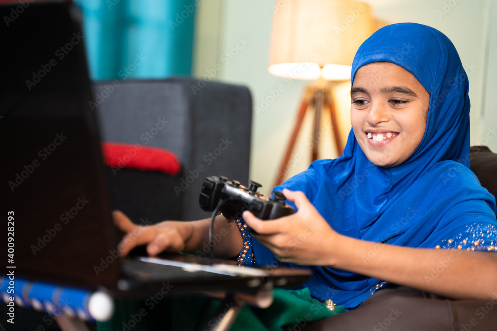 Happy smiling Muslim Girl Kid playing online videogame on laptop by ...