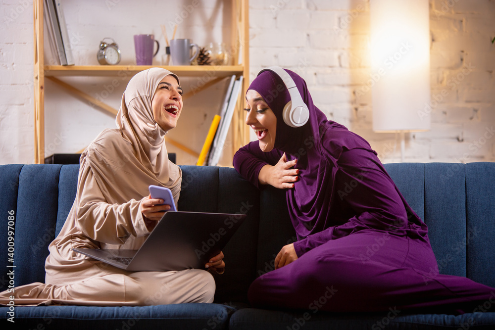 Laughting. Happy and young two muslim women at home talking, smiling ...