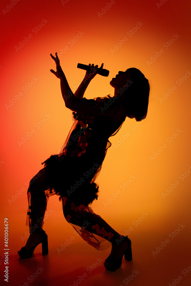 Dance. Silhouette of young female singer isolated on orange gradient ...
