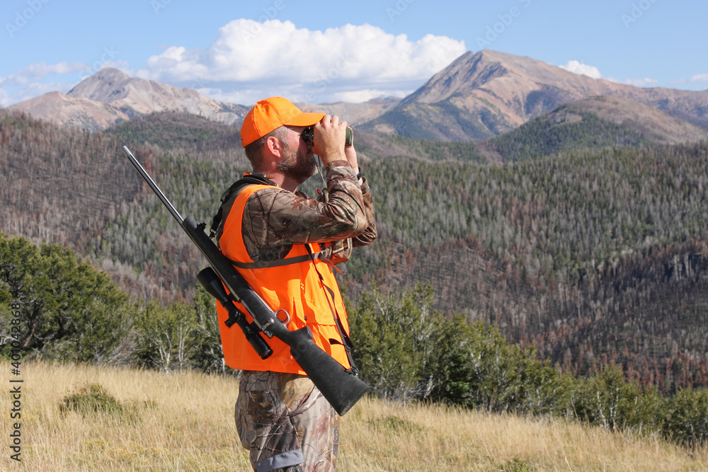 adult male deer hunter looking through binoculars in rugged mountains ...