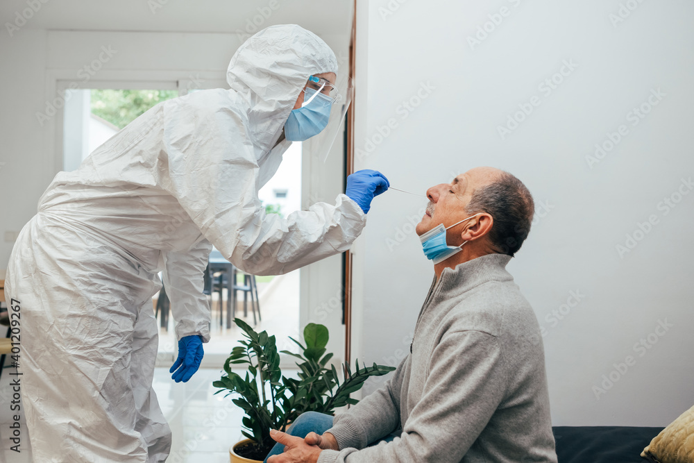 Health Professional in PPE suit and face shield introducing a nasal ...