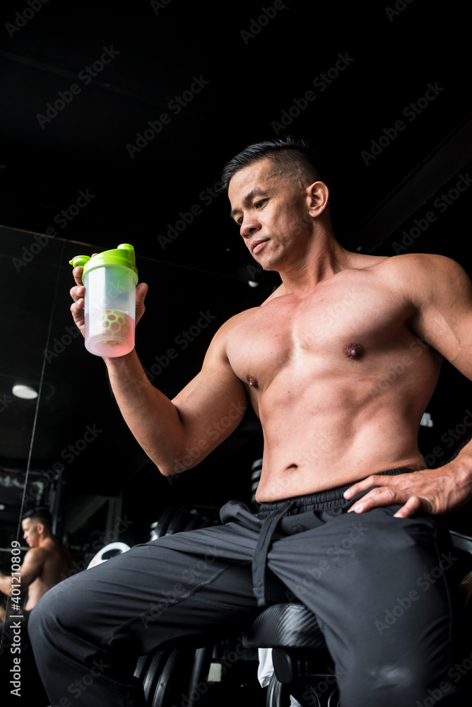 A fit asian man checks out remaining sports drink after a vigorous ...