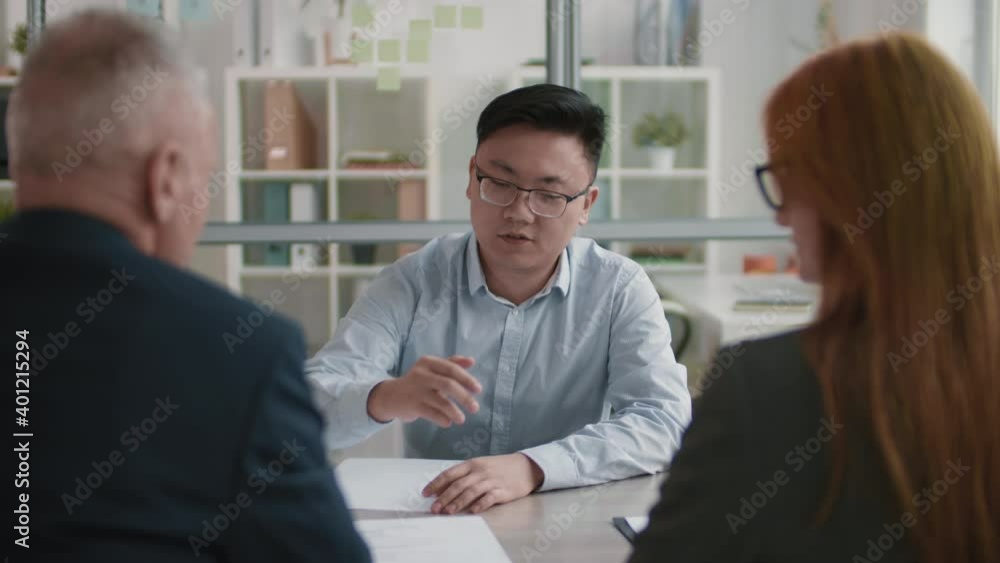 Rear view of red-haired manager and male colleague sitting by desk in ...