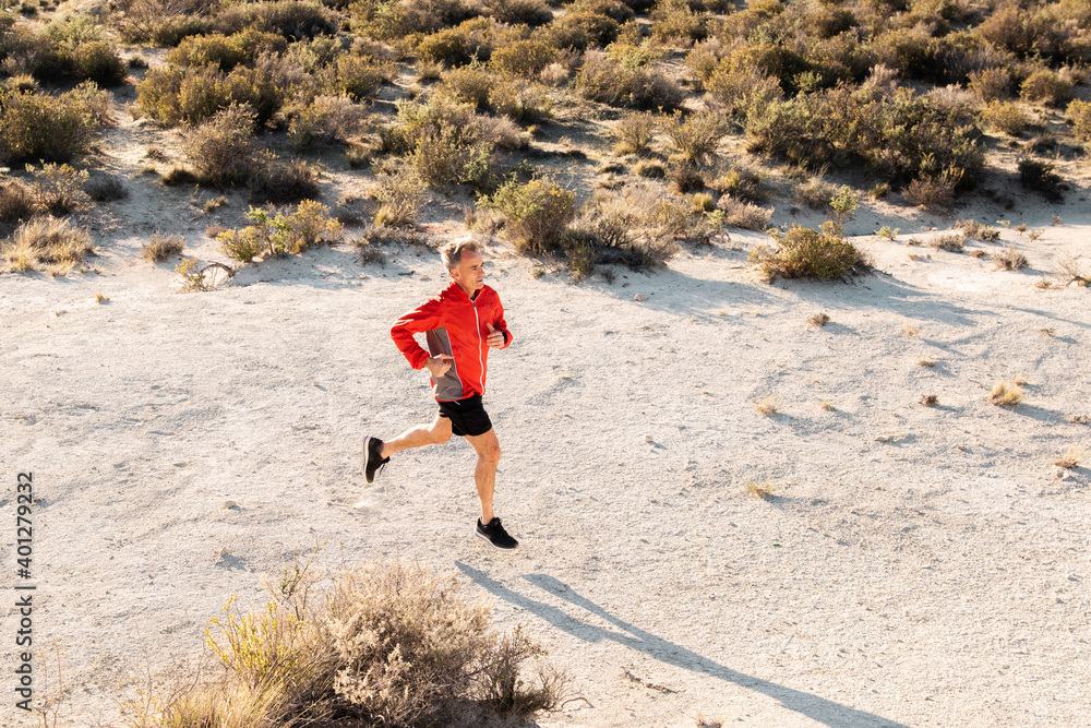 From above of active male jogger running uphill in sandy semi desert ...