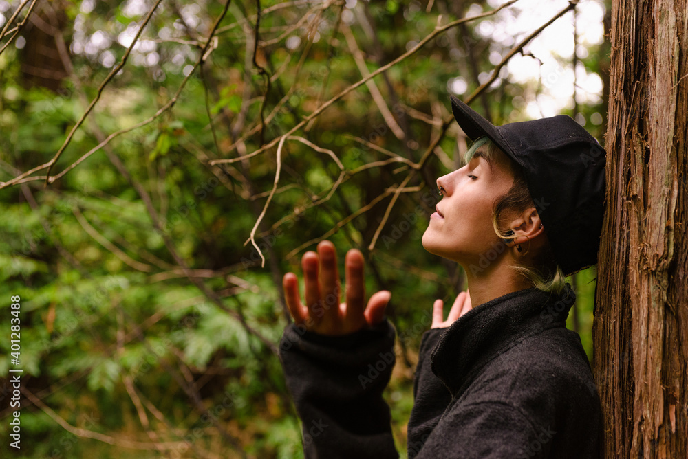 Side view of serene female standing with closed eyes in woods and ...