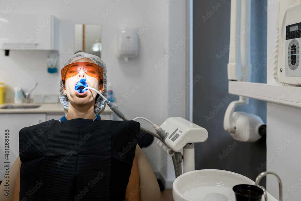 Female patient in laser safety goggles with dental expander and saliva ...