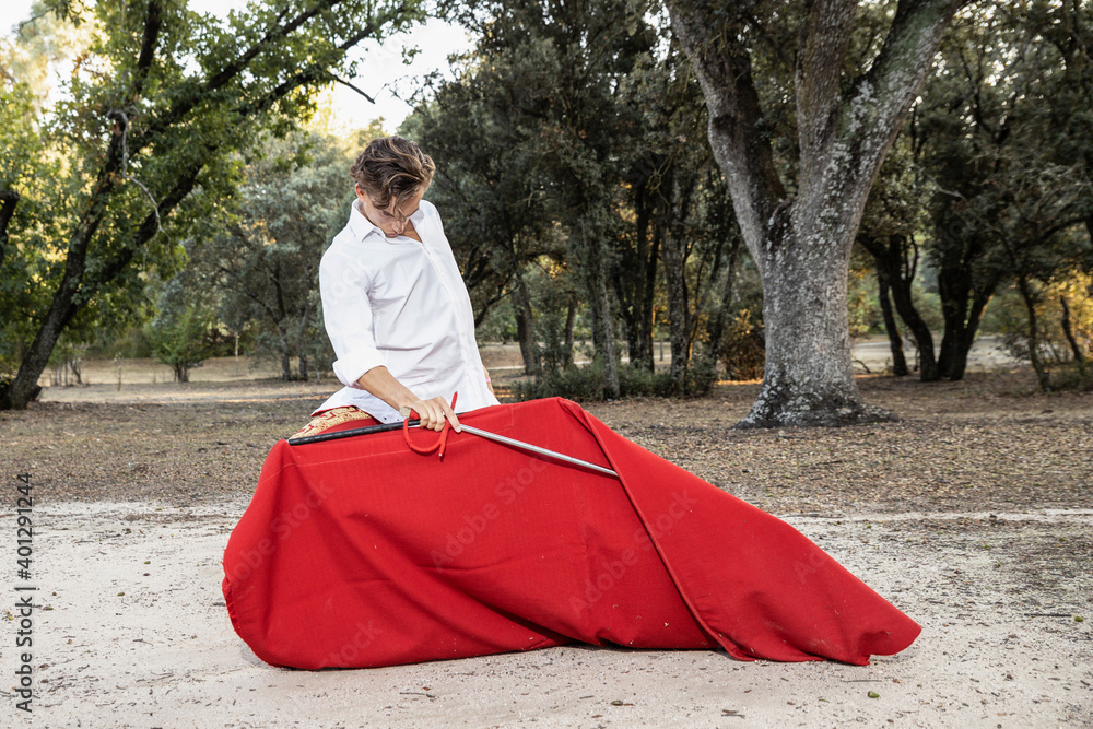 Serious slim male bullfighter in red pants and white shirt holding ...