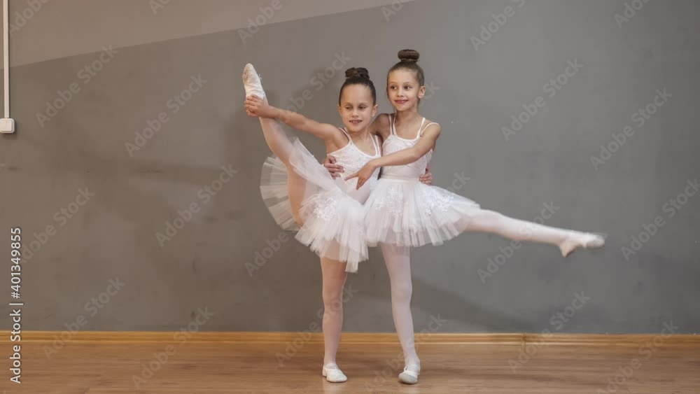 Two flexible little ballerinas are standing in the vertical splits in a ...