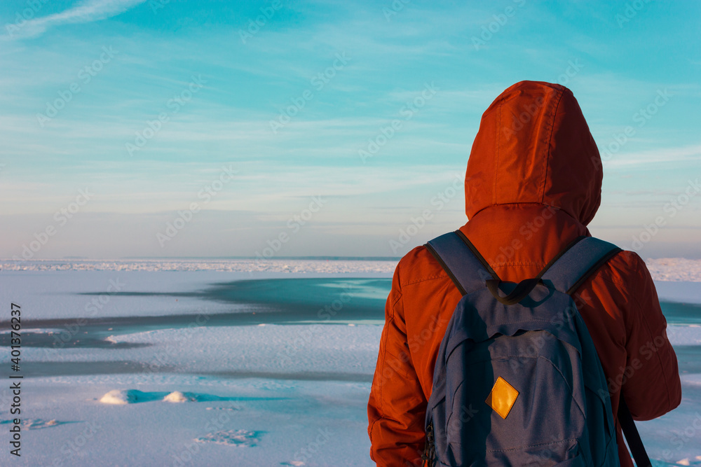 Back view of male tourist with rucksack standing on coast of the frozen ...
