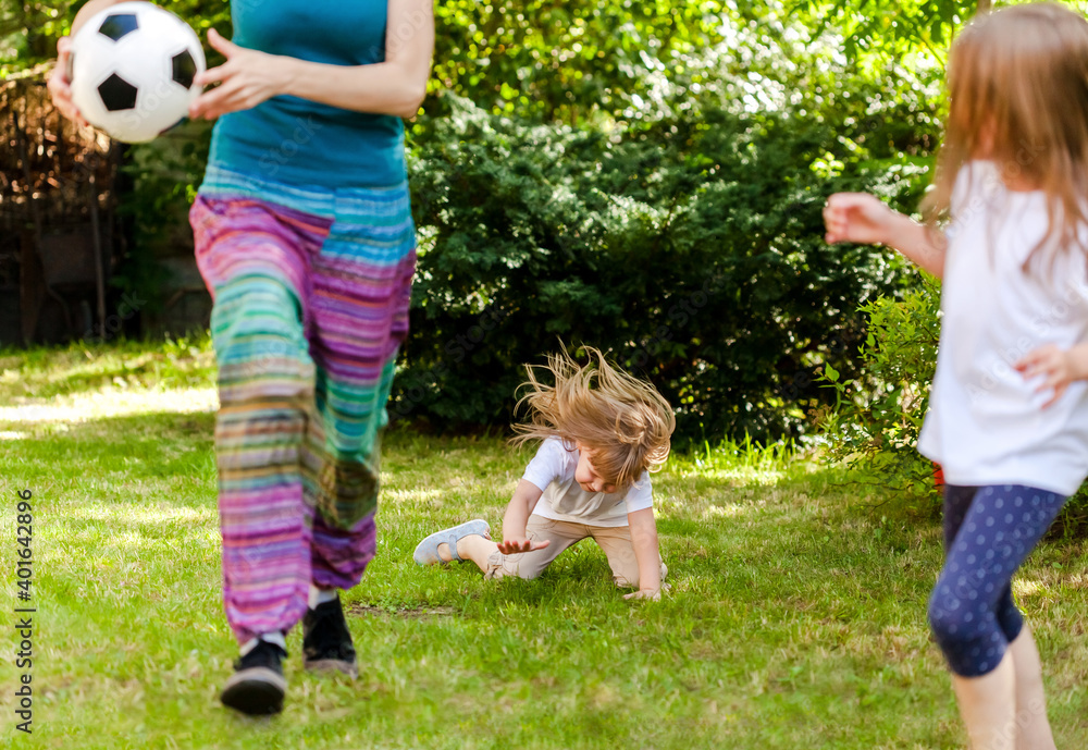 Child falling down running, playing ball with family in the garden ...